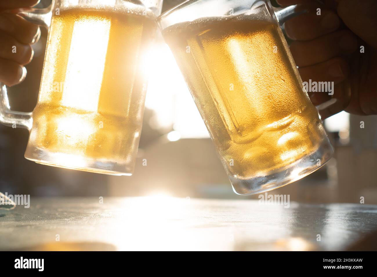 Closeup toast clinking fresh lager beer mugs with sun rays in hot ...
