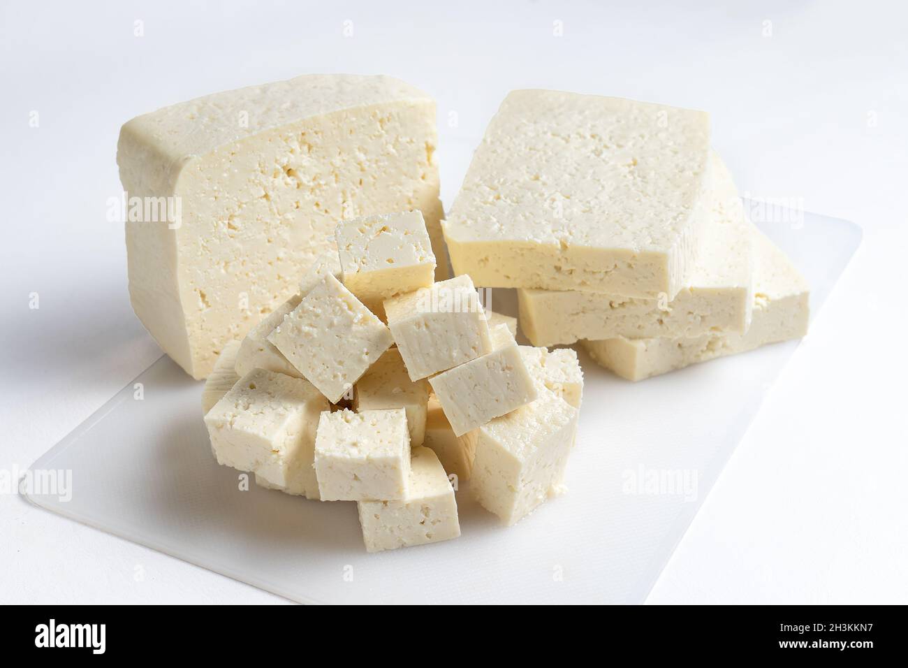 White cheese cut into several pieces on a white surface and white ...