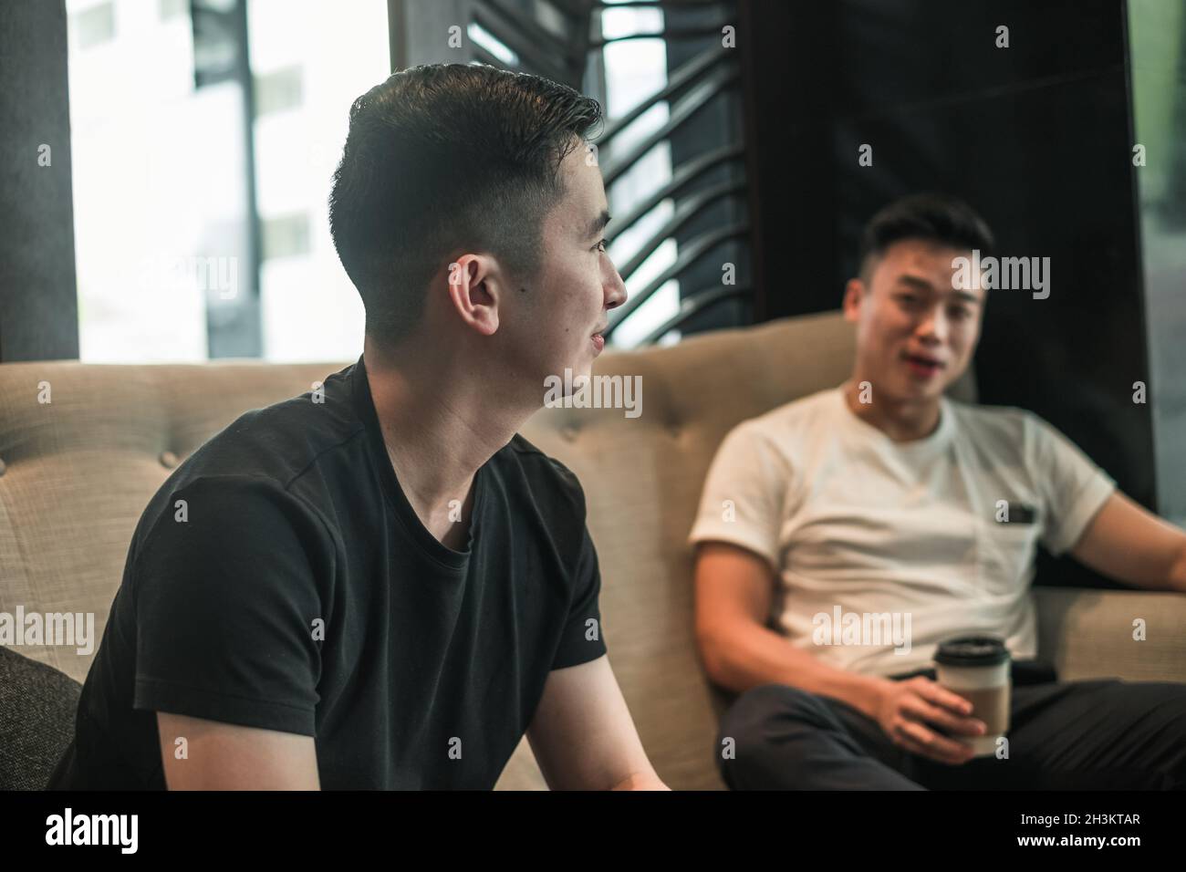 Two asian young men sitting in coffee shop, drinking coffee, talking ...