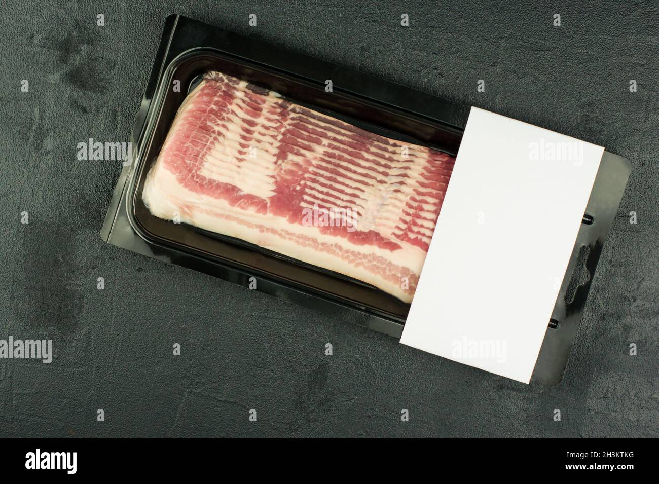 smoked pork bacon in factory plastic packaging on a black background ...