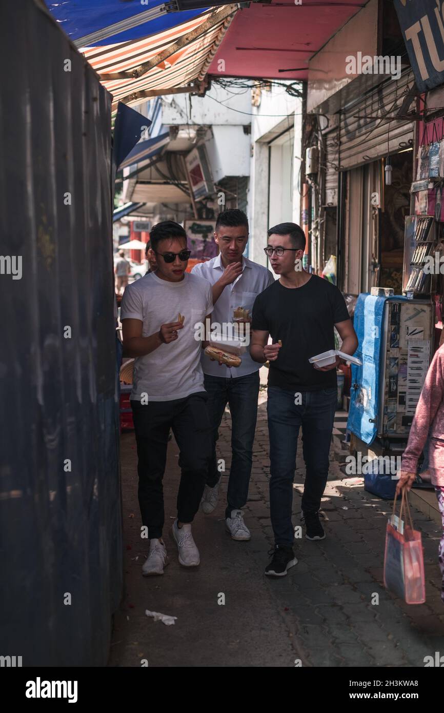 Three asian men walking on the street and eating fast food. Asia ...
