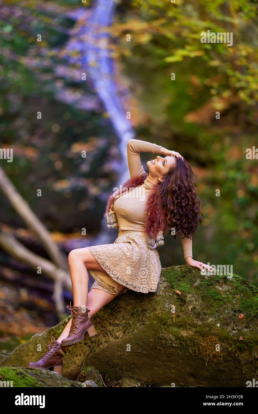 a beautiful woman sitting by a waterfall in different positions during ...