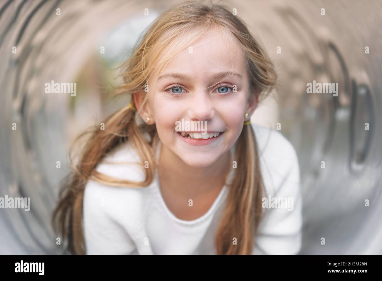Pretty, little girl, having fun, lying on pipe on children playground ...