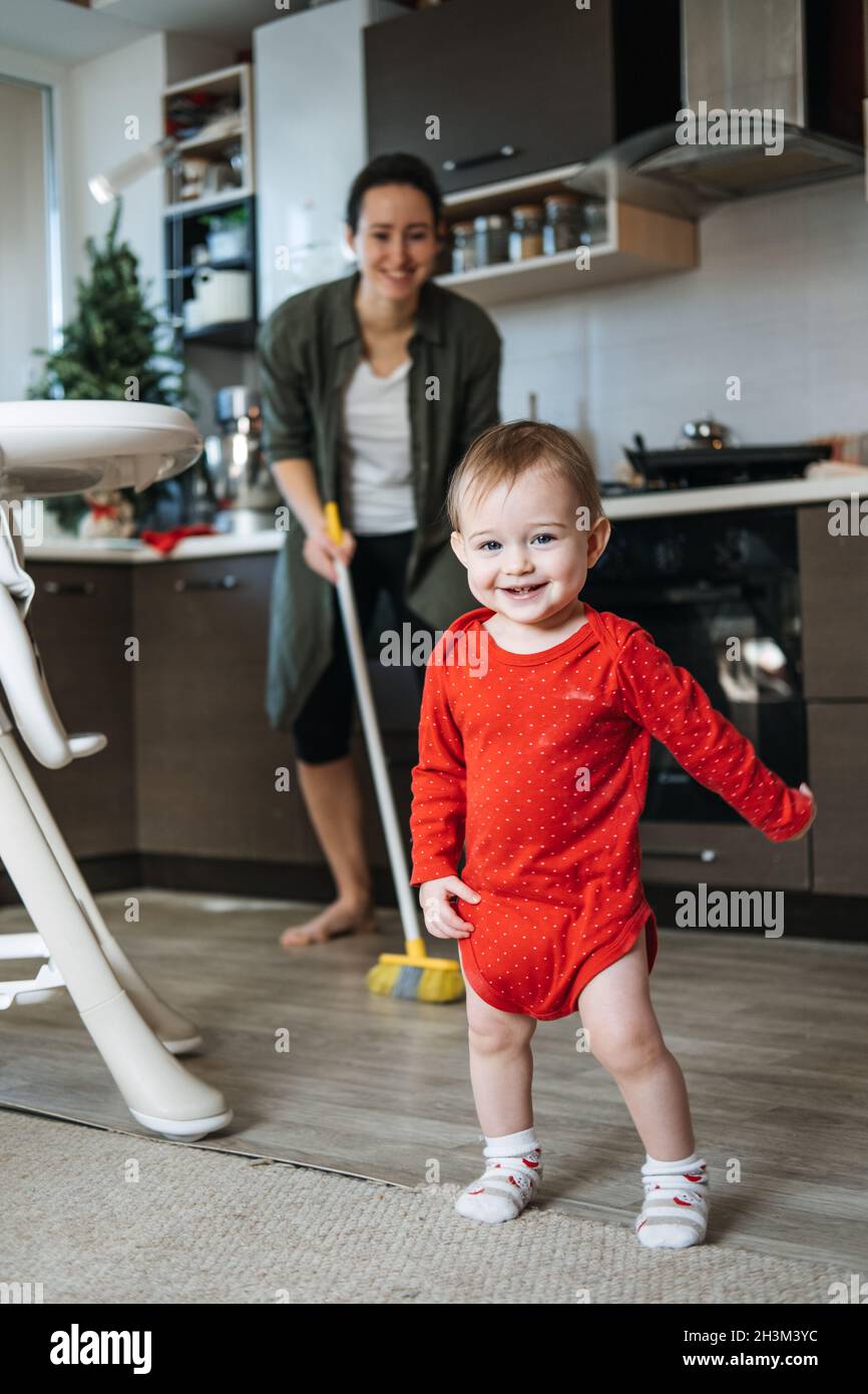 Little mothers helper. Cute toddler baby girl with mop help her mom do ...