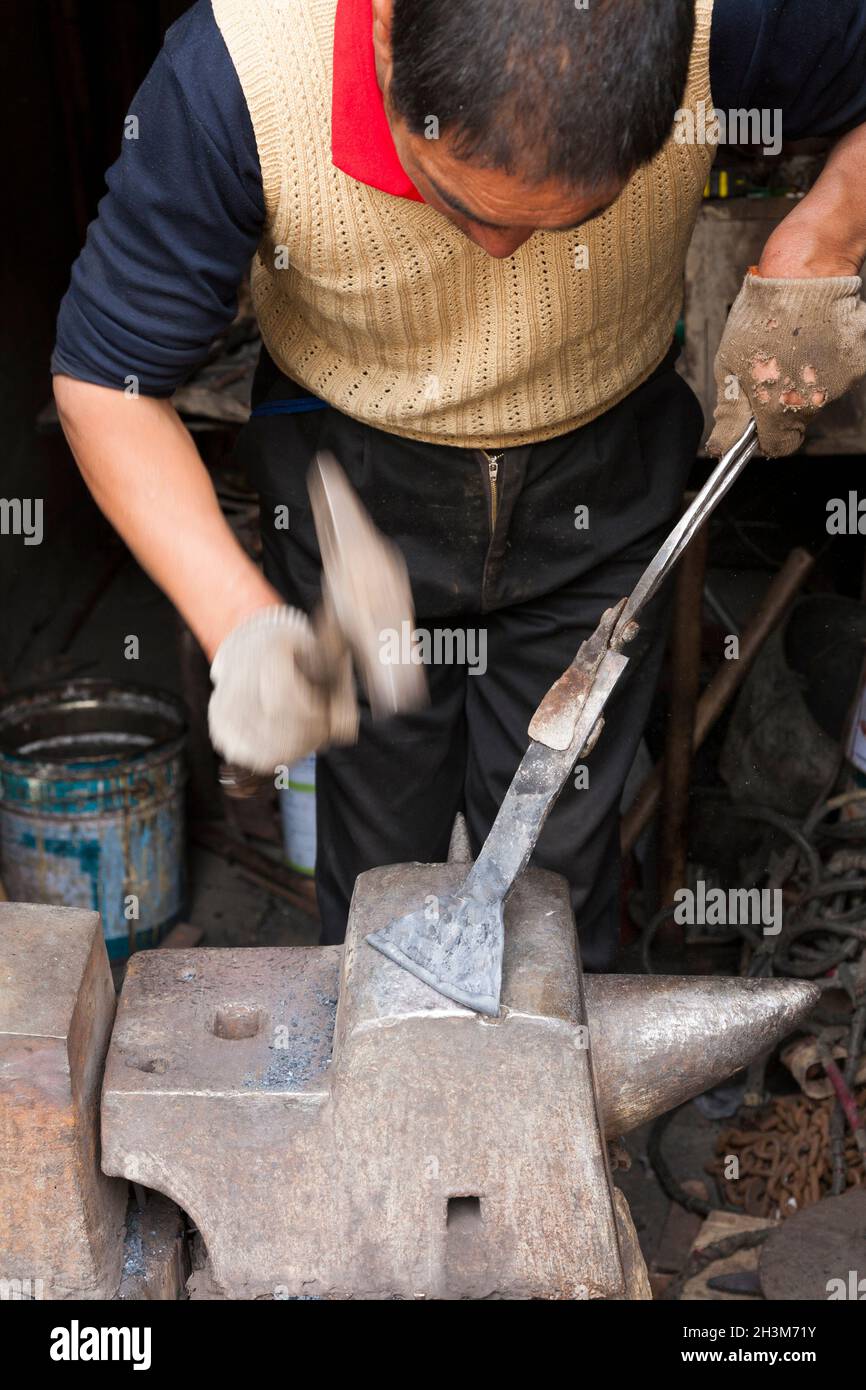 Worker / metalworker black smith working beating hot metal on an anvil ...