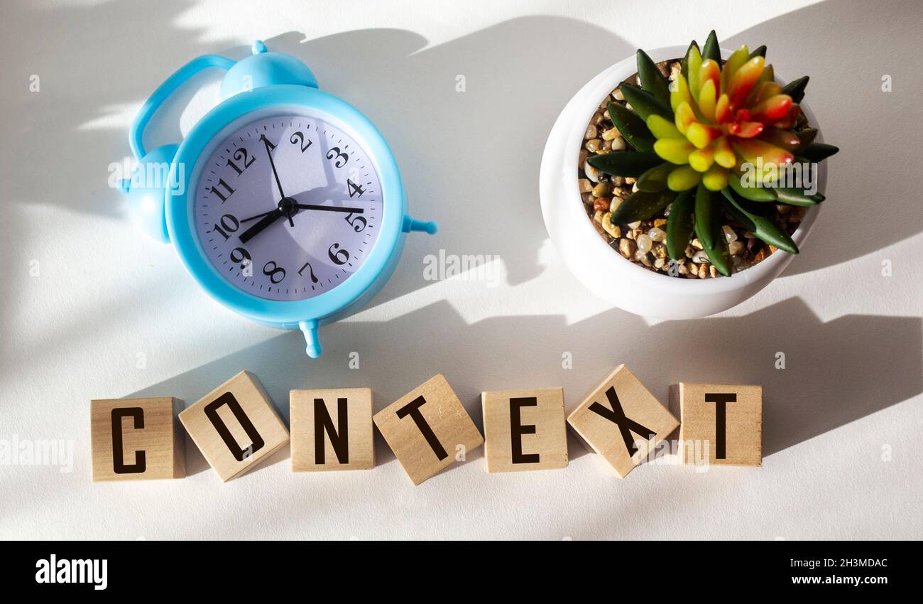 Context word in wooden cube with alarm clock and cactus flower on white ...