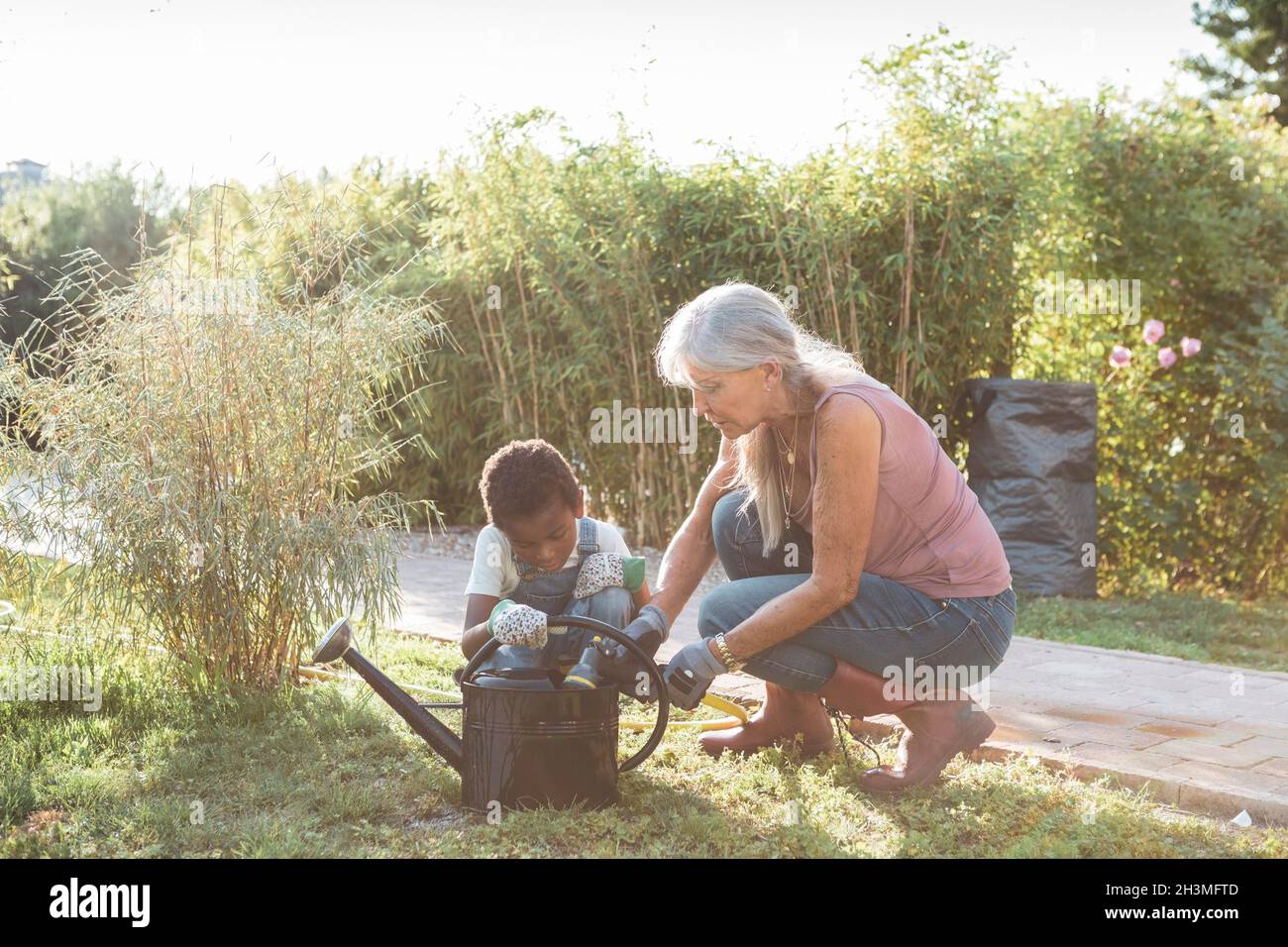Boy and grandmother crouching with watering can at farm Stock Photo - Alamy