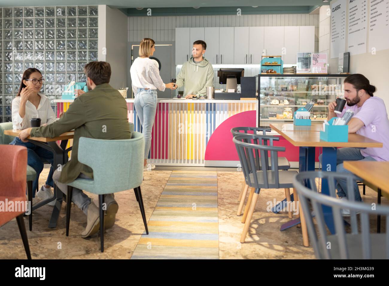 Female client taking order from barista near other customers in modern ...