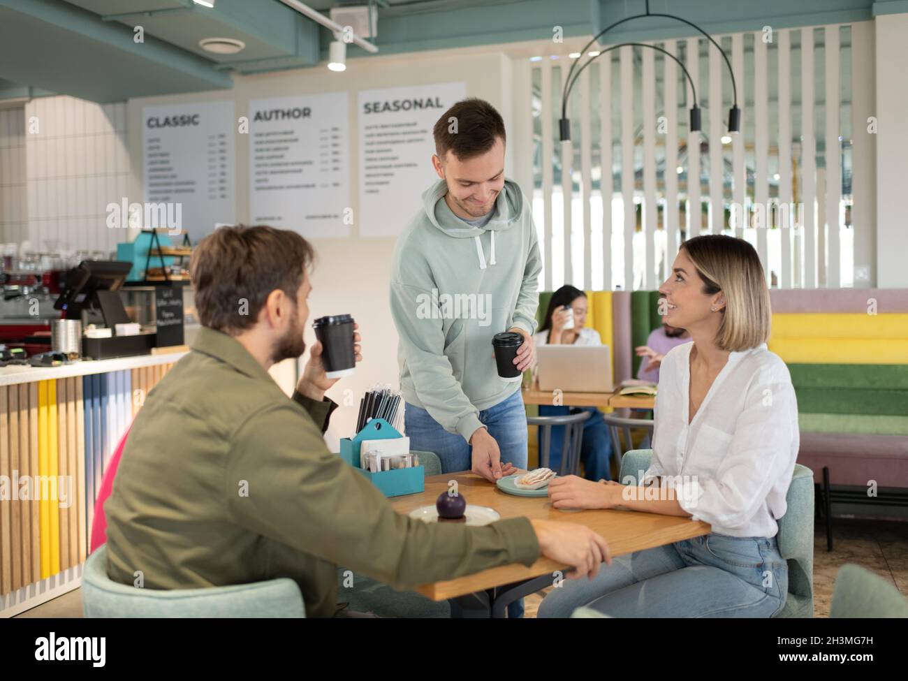 Friendly male waiter serving coffee and dessert to couple while working ...