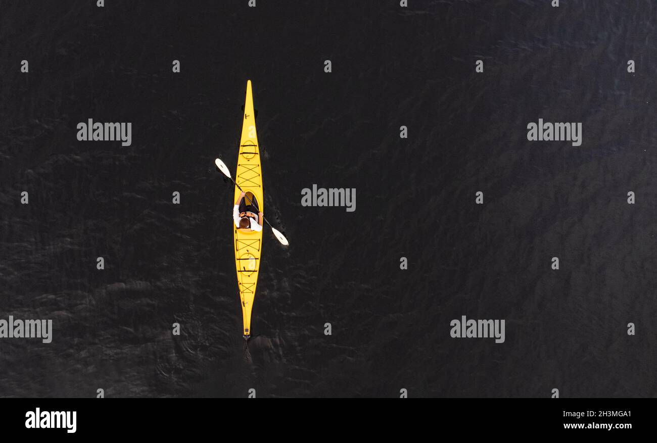 Aerial view of woman paddling yellow kayak on dark lake water Stock ...