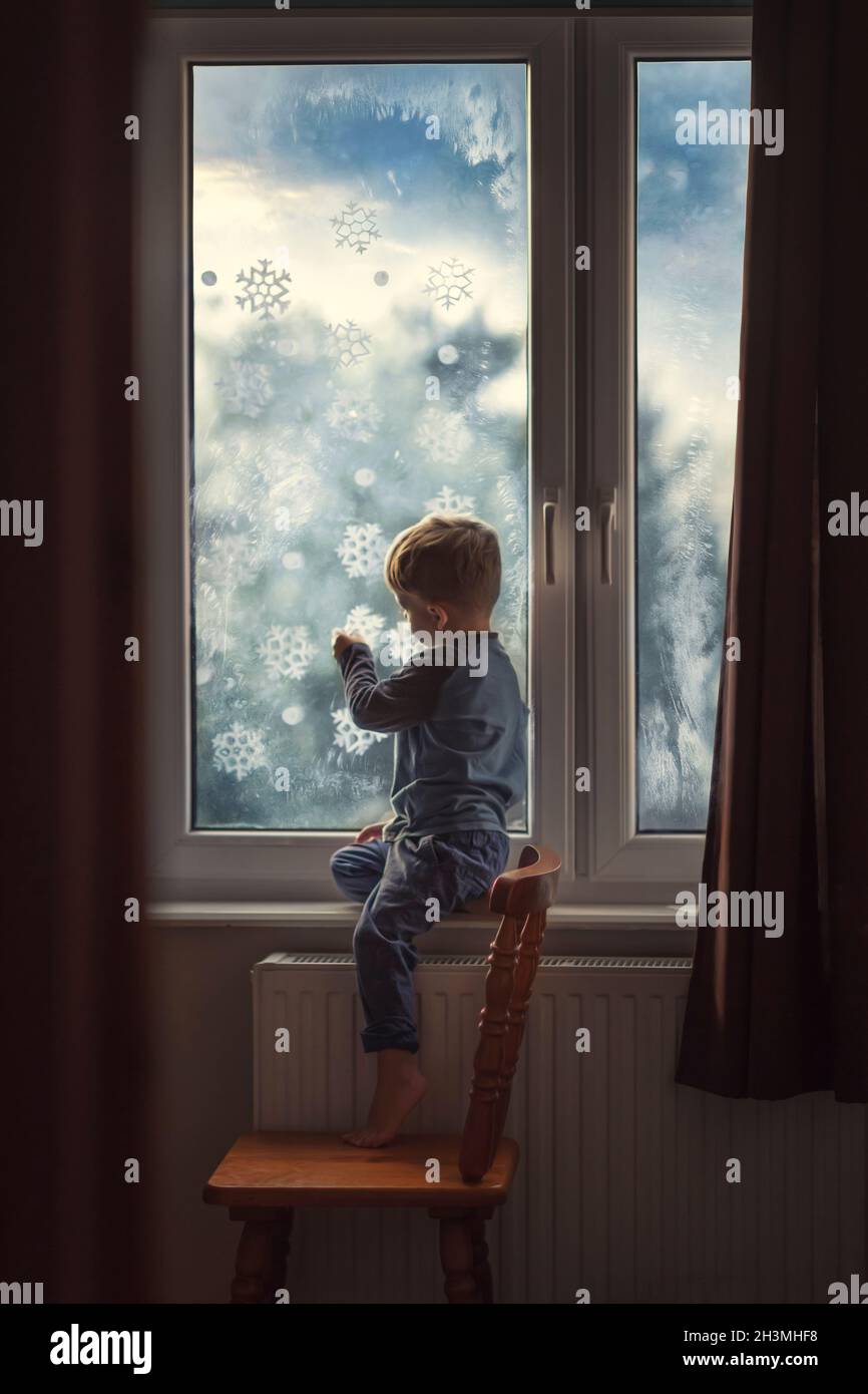 Small boy in blue clothes sitting on window sill and attaching c Stock ...