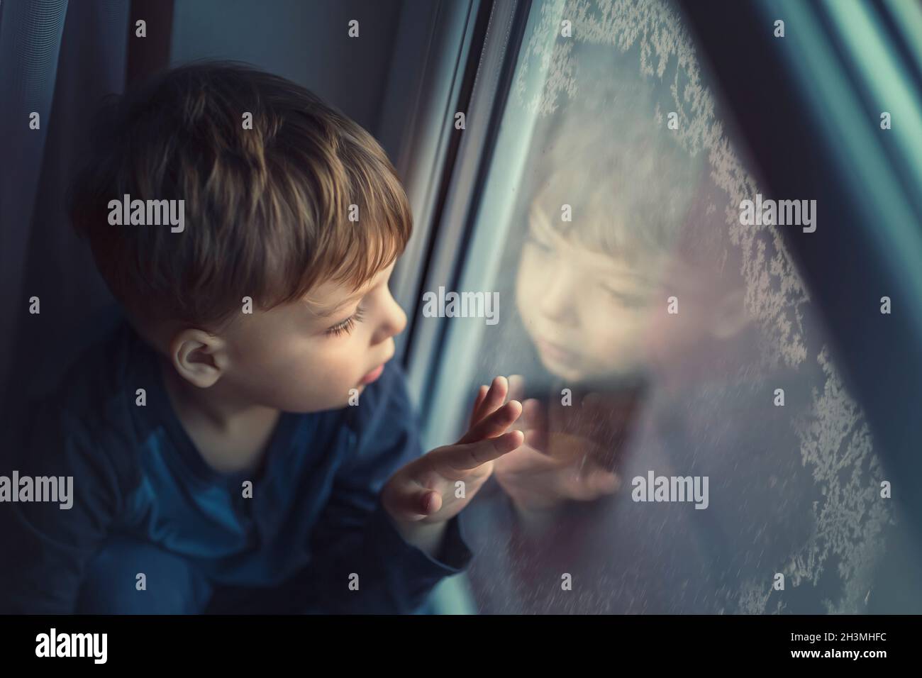 Small boy looking on frozen window and seeing his own reflection Stock ...