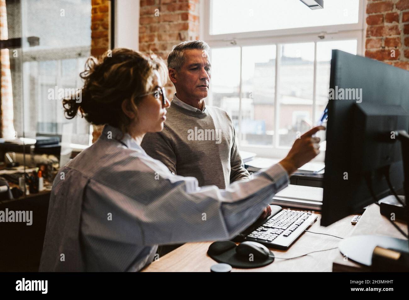 Female professional explaining businessman while pointing on computer ...