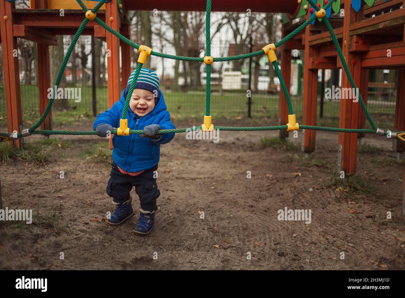 Toddler boy laughing on playground wearing blue winter clothes Stock ...