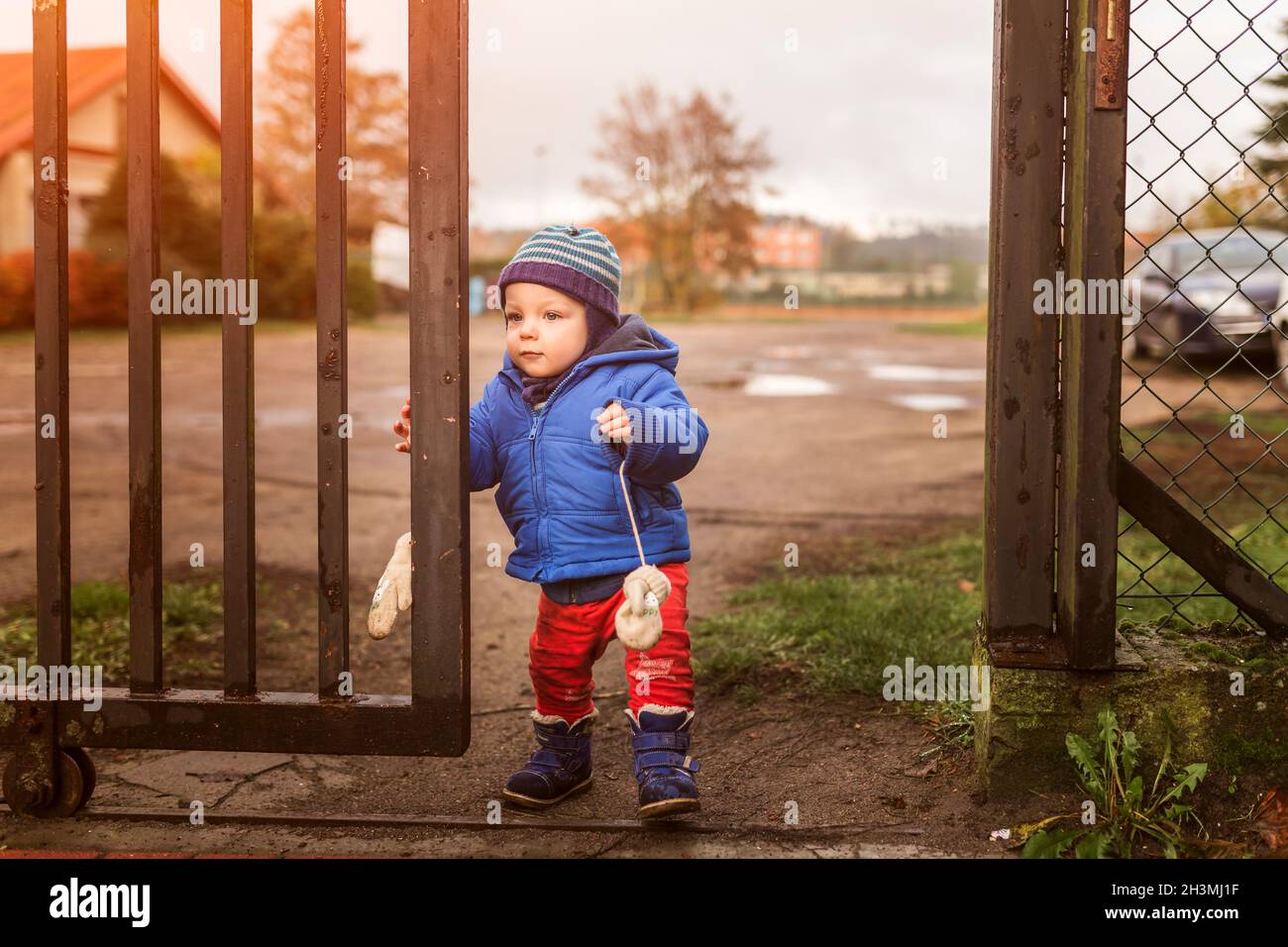 Small boy walking through gate wearing blue jacket and red trous Stock ...
