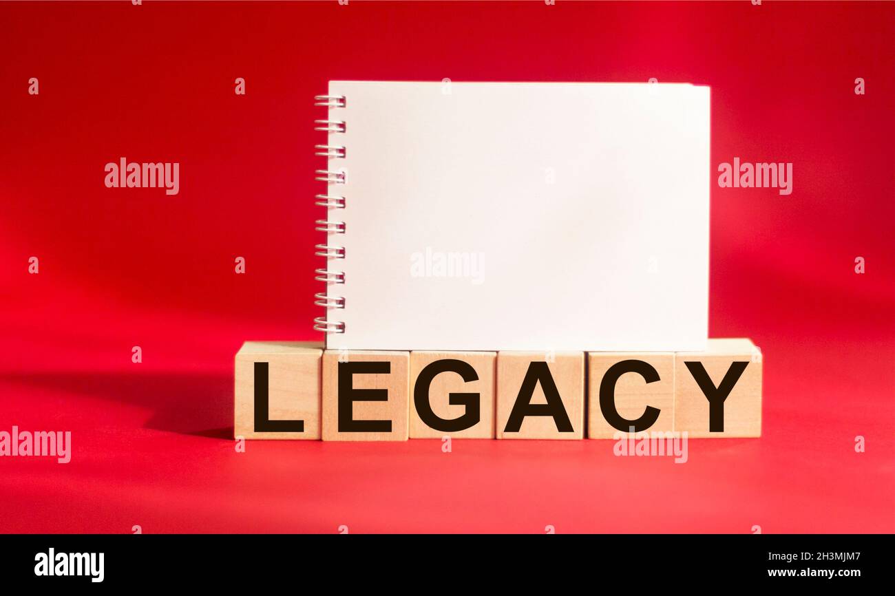 LEGACY text on wooden cubes on a red background and with a notepad to ...