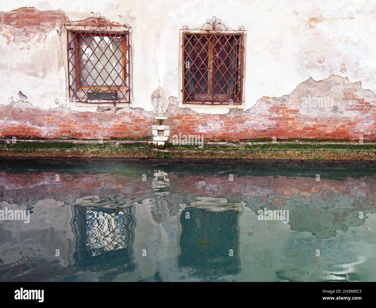 Two ornate windows with rusting iron bars in an ancient white plastered ...