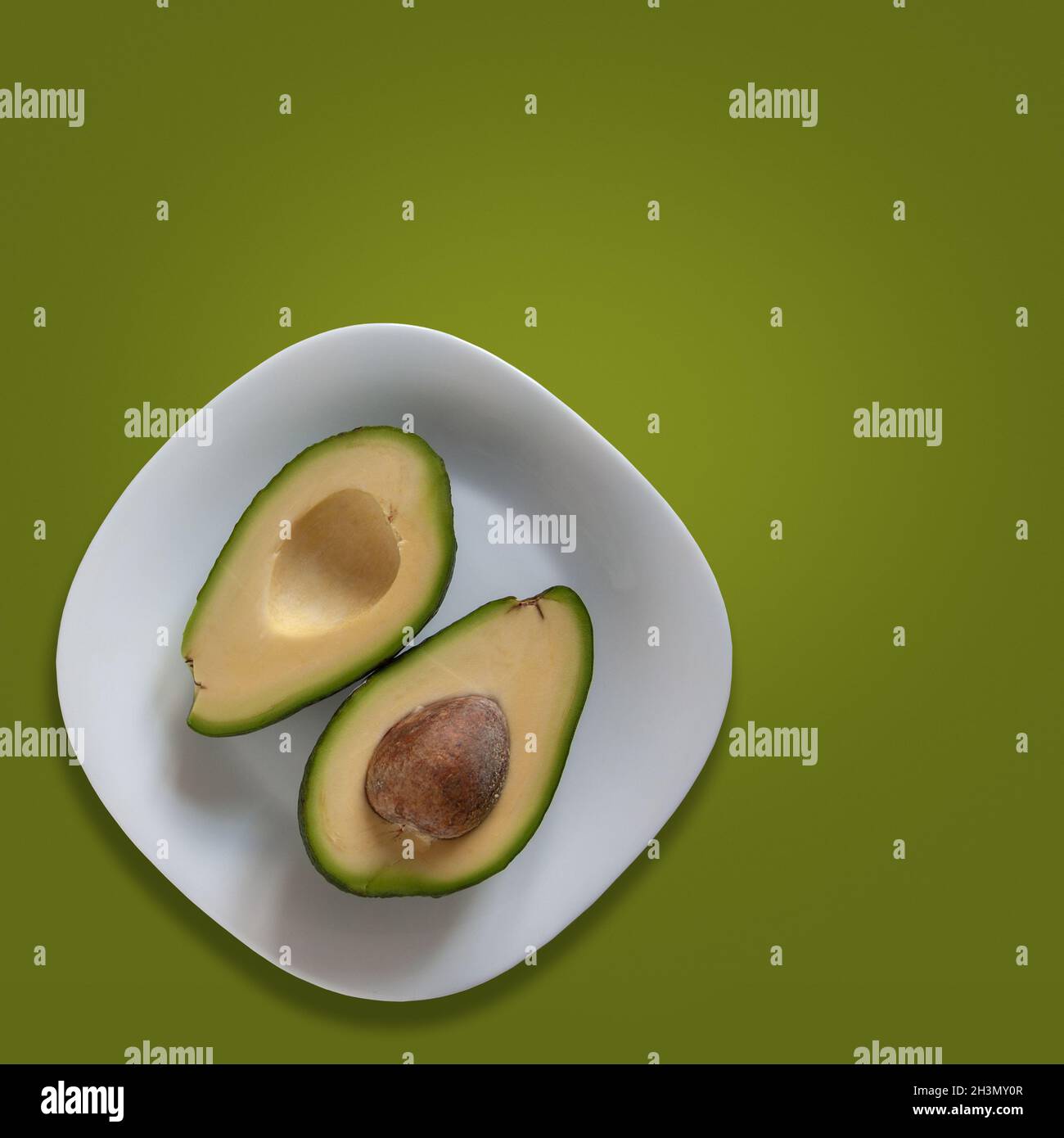 Fresh avocado. Two halves on white dish. Cut out on green background ...
