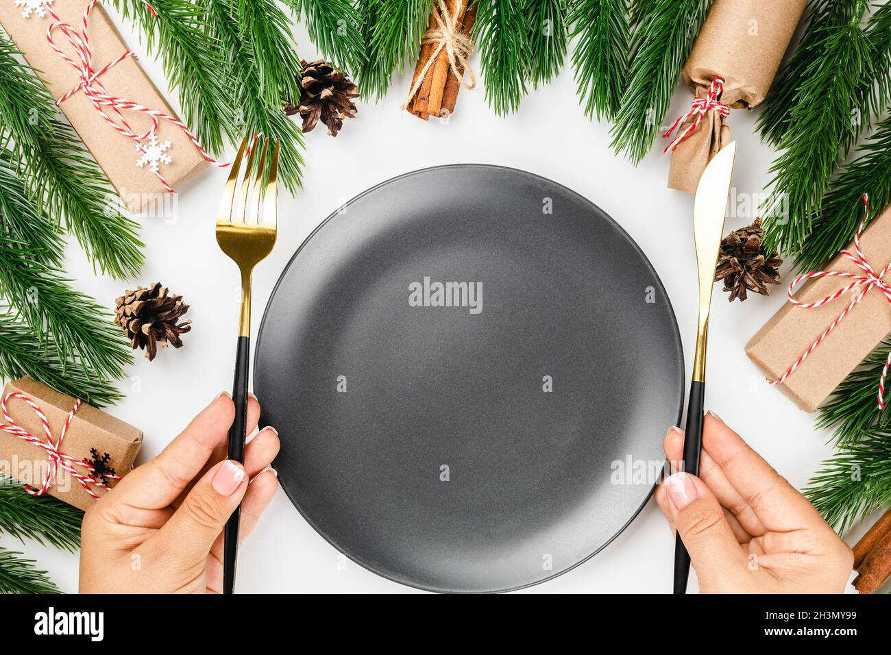 table set for Christmas party. Woman hands hold gold cutlery over black ...
