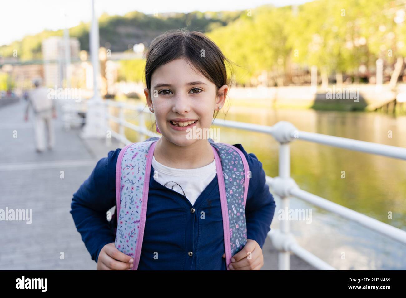Portrait of smiling little girl carrying school backpack by river walk ...