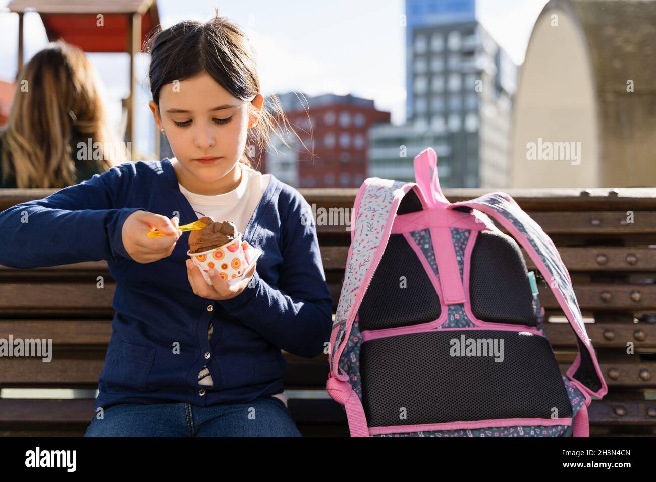 Little girl enjoying ice cream sitting on park bench on sunny day ...