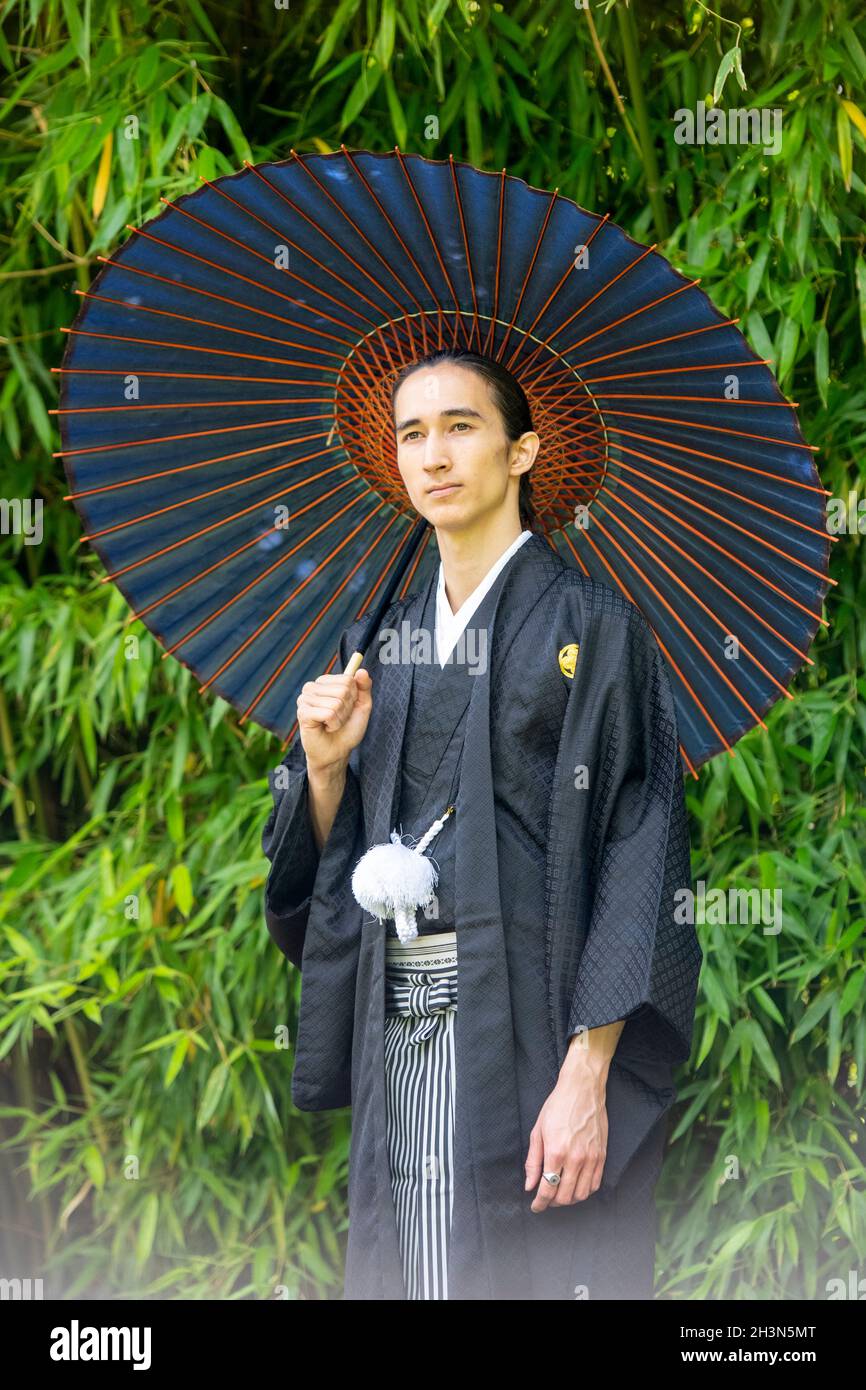 UK, Portrait of young man wearing kimono holding parasol in park Stock ...