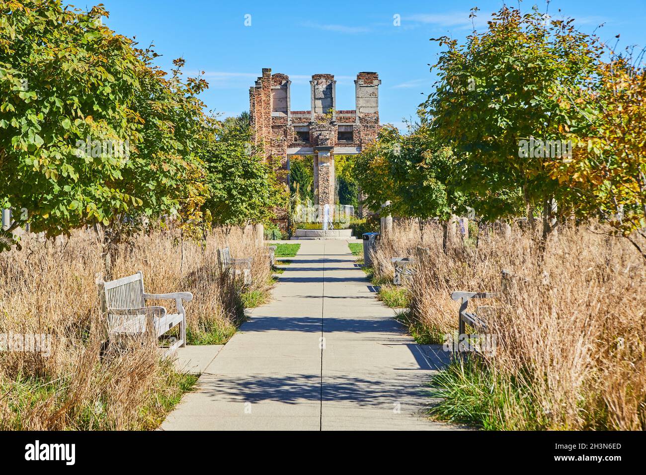 Old ruins at end of long walkway lined with benches and fall grasses ...