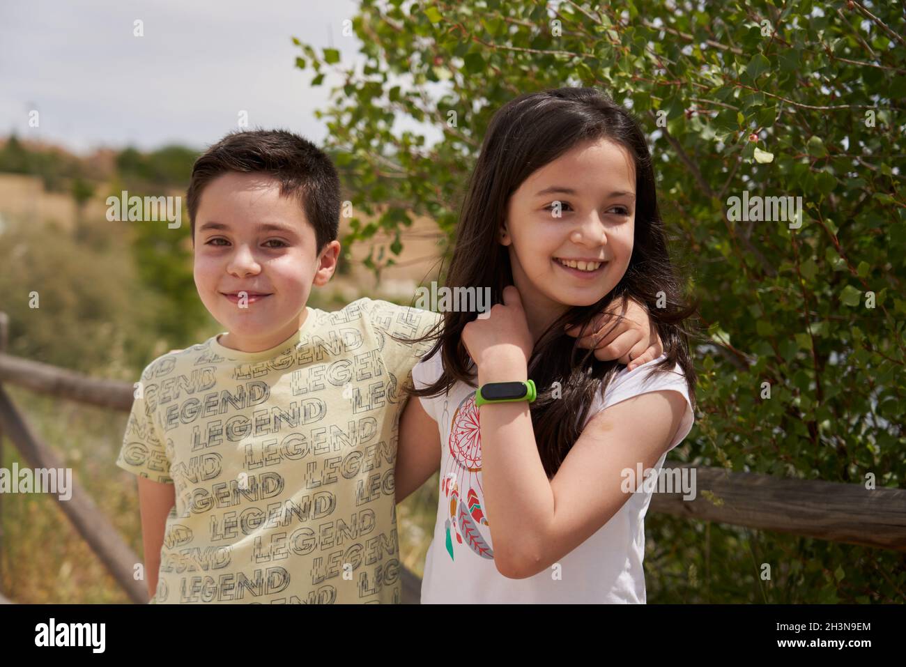 Children embraced smiling happily in a park with wooden fence behind ...