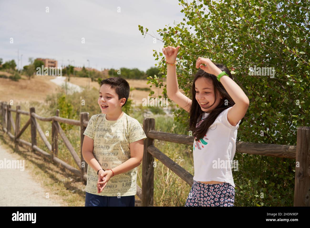 Children playing laughing happily in a park with wooden fence behind ...