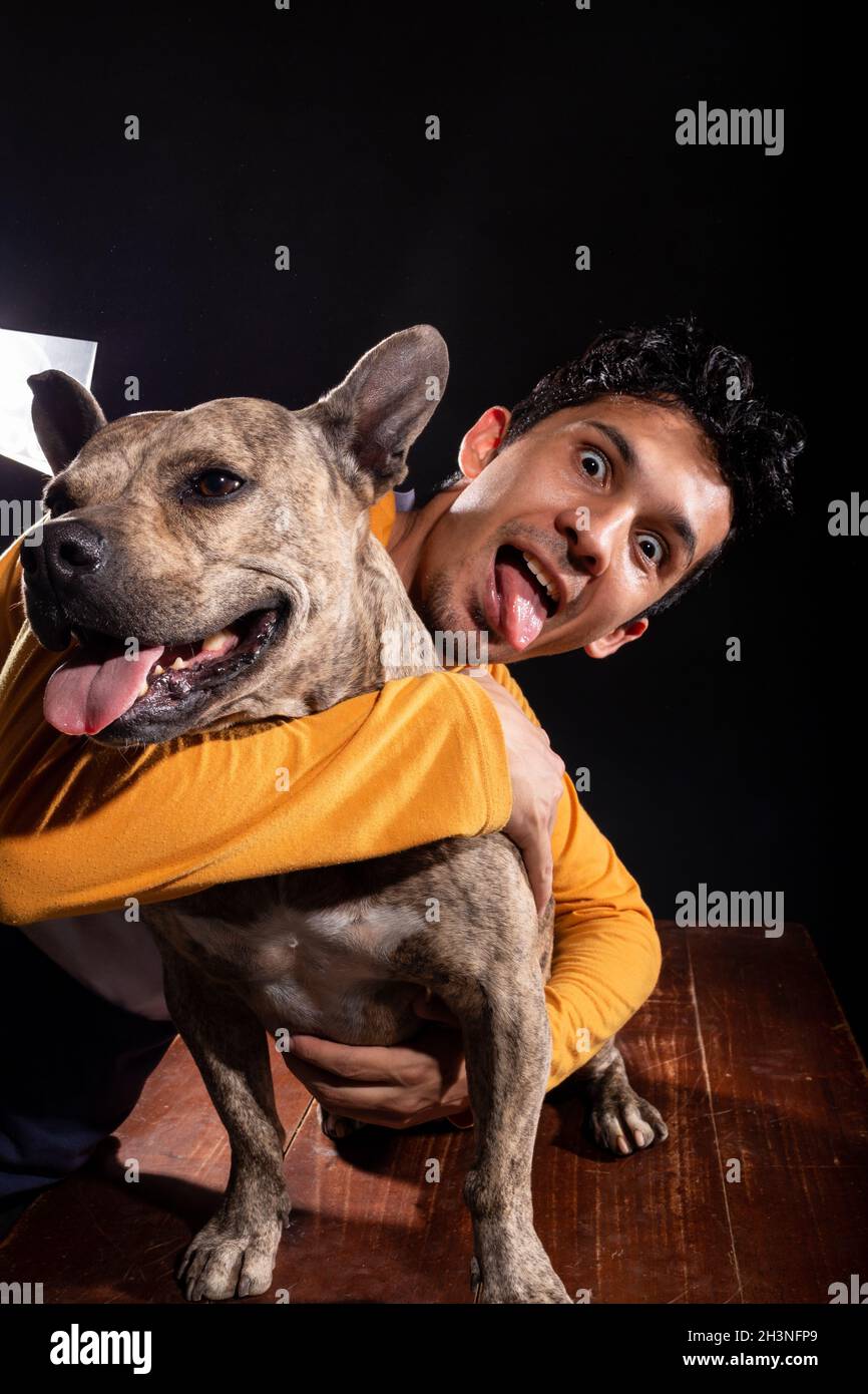 latin man hugs dog. isolated on black background. sticking out tongue ...