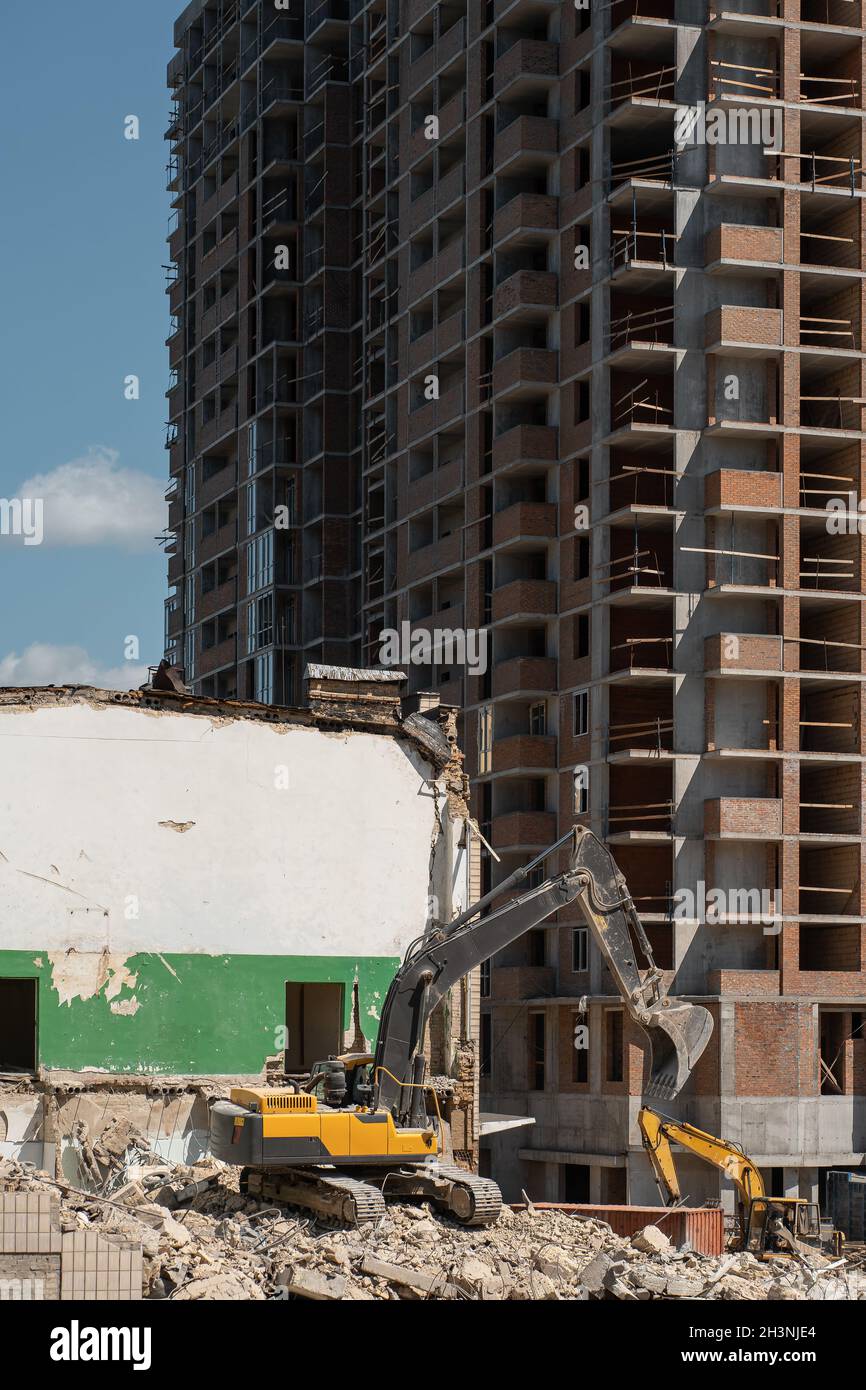 demolition old building by excavator near new construction of modern ...