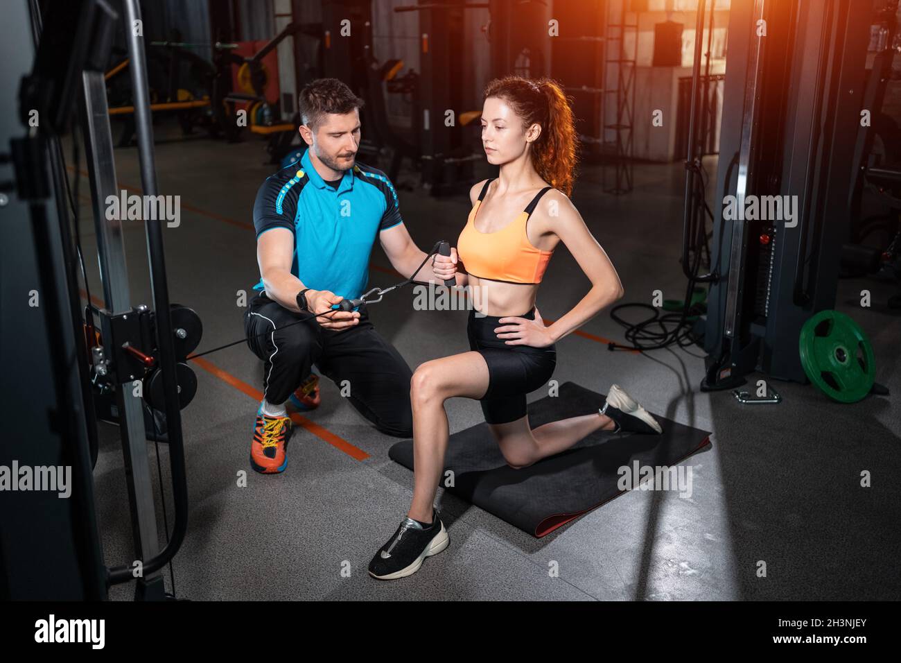 young woman exercising single arm row kneeling with personal trainer ...