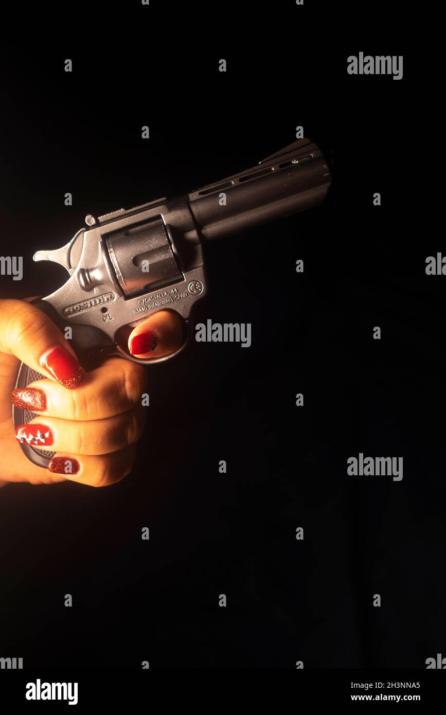 Lady spy detective with painted red nail varnish holding pistol gun at ...
