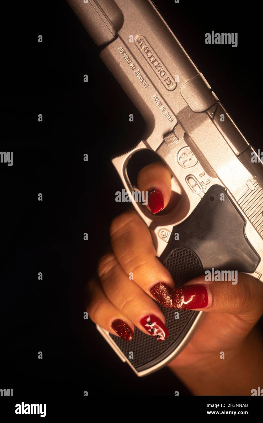 Lady spy detective with painted red nail varnish holding pistol gun at ...