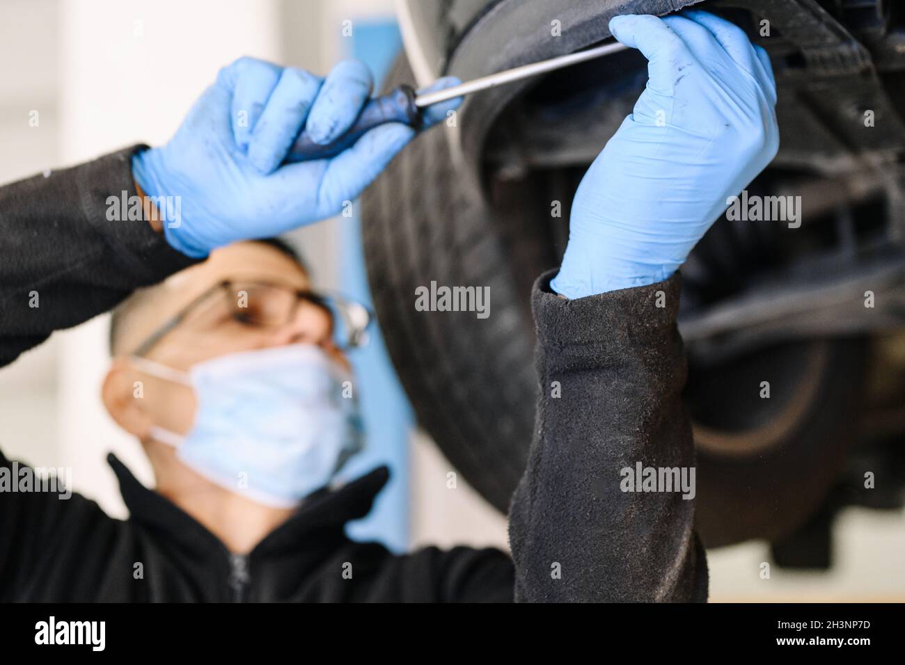 Professional mechanic with protective face mask, repairing a car in ...