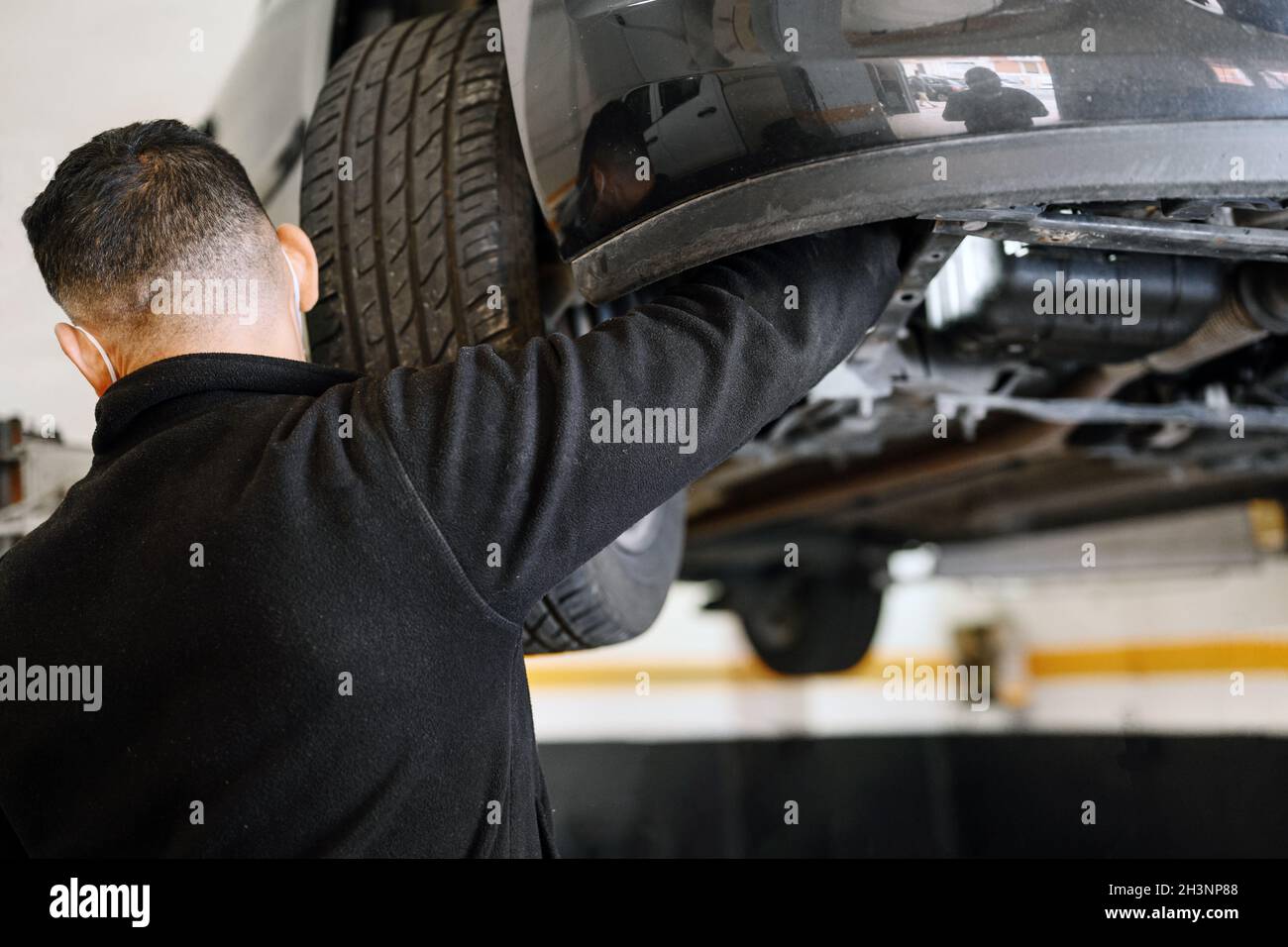 Professional mechanic with protective face mask, repairing a car in ...