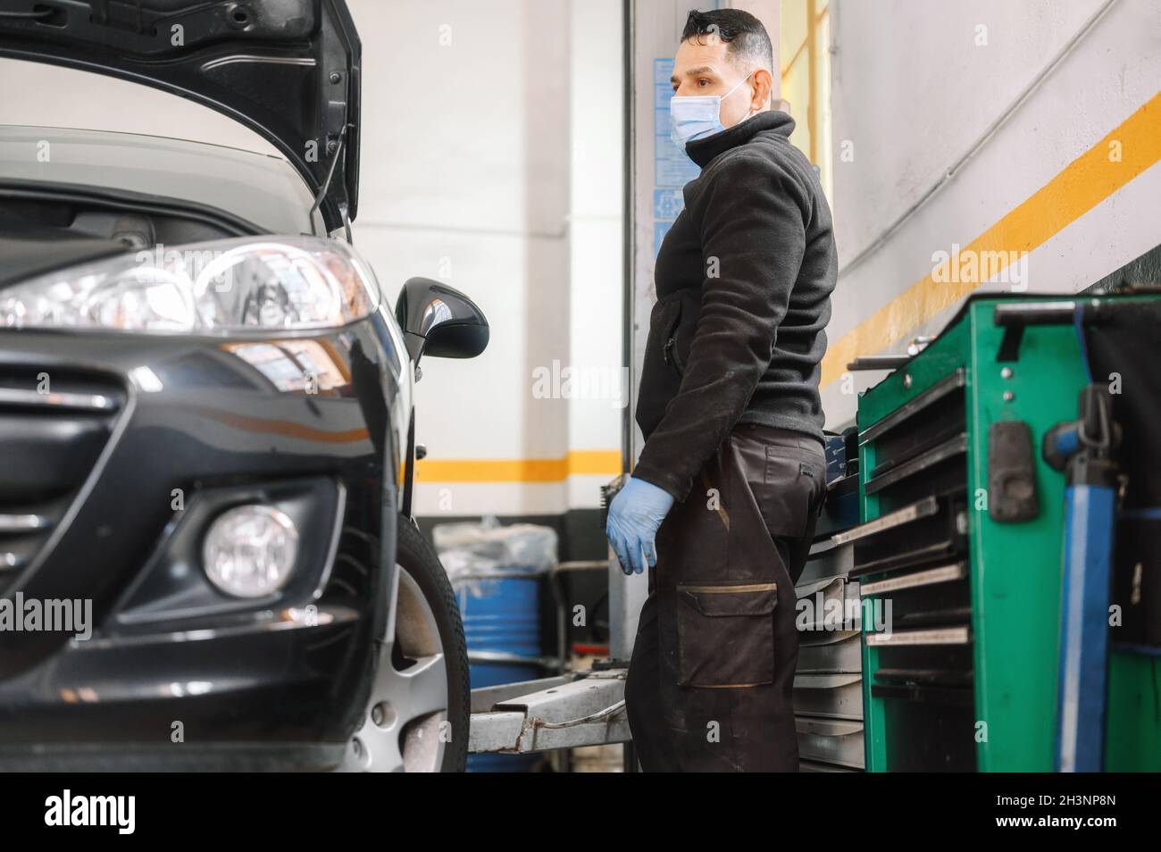 Professional mechanic with protective face mask, repairing a car in ...