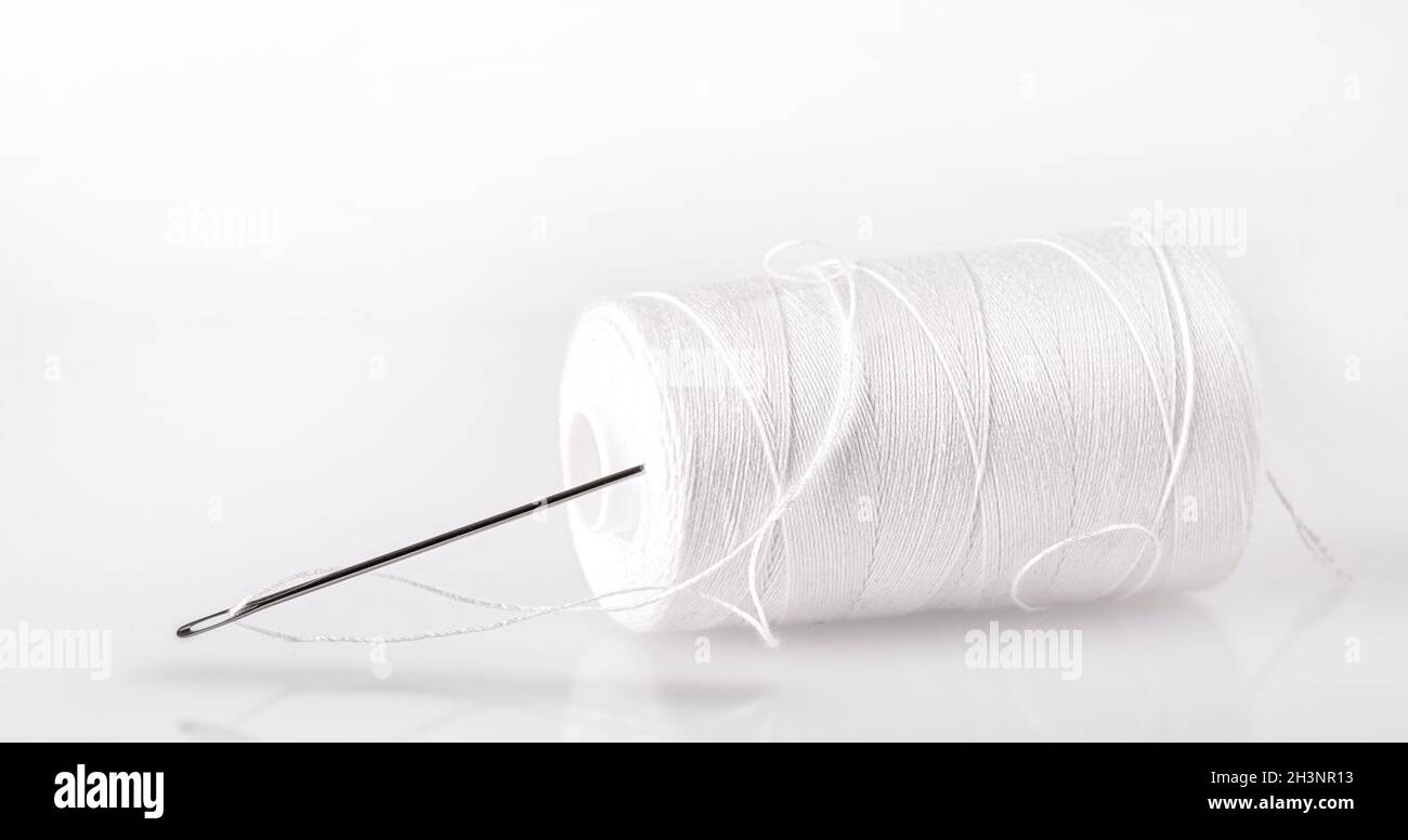 spool with white thread and a needle Stock Photo - Alamy
