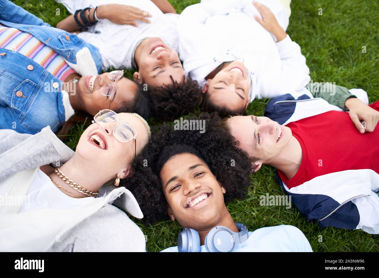Group of friends laughing outdoors lying on the grass, sharing a good ...