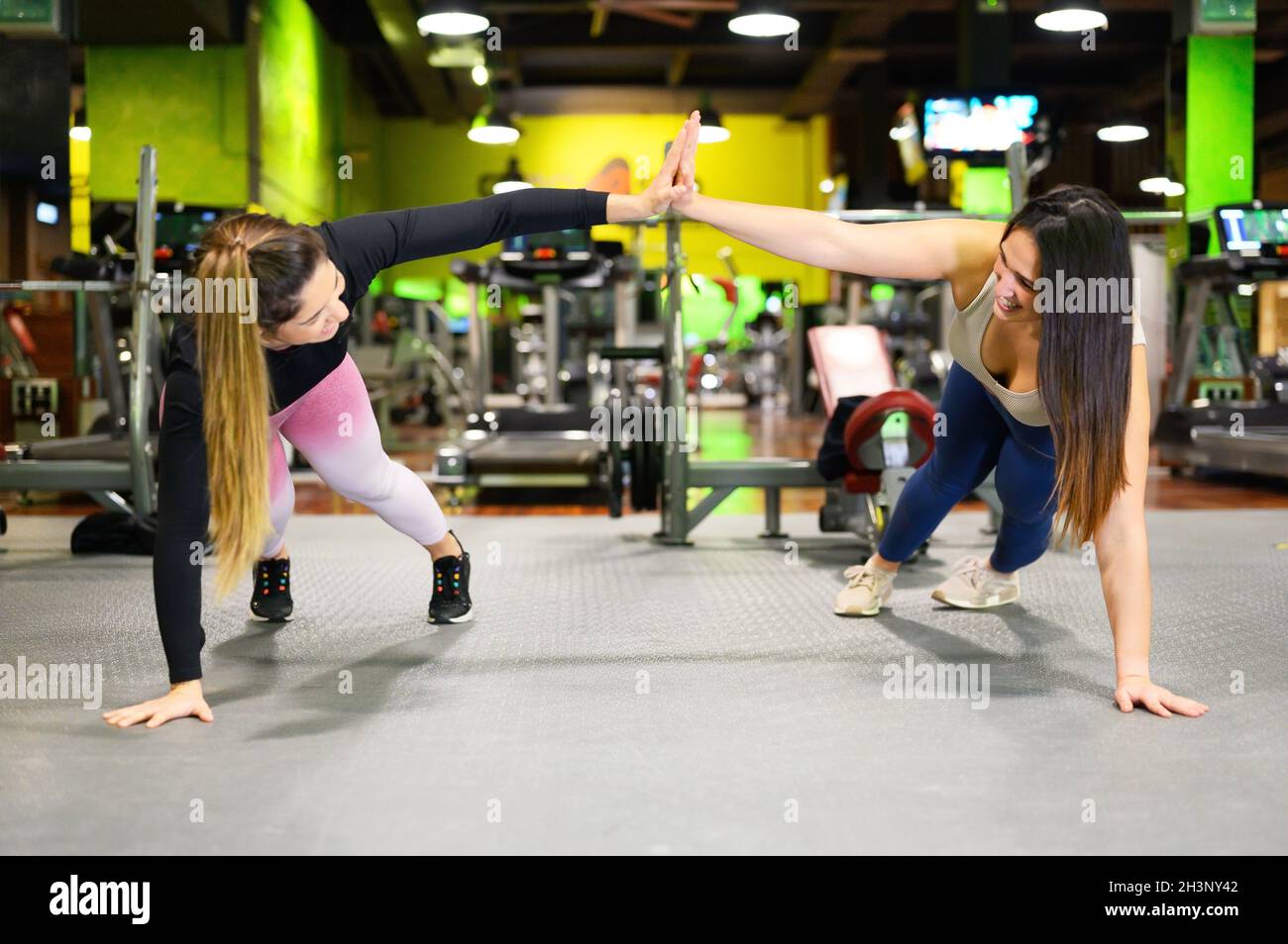 Two sporty women doing high five while workout push up exercise in Gym ...