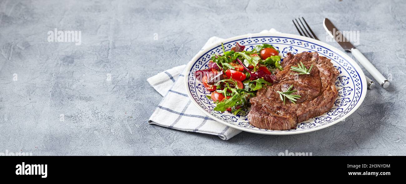Grilled steaks and vegetable salad on light background. Table setting ...