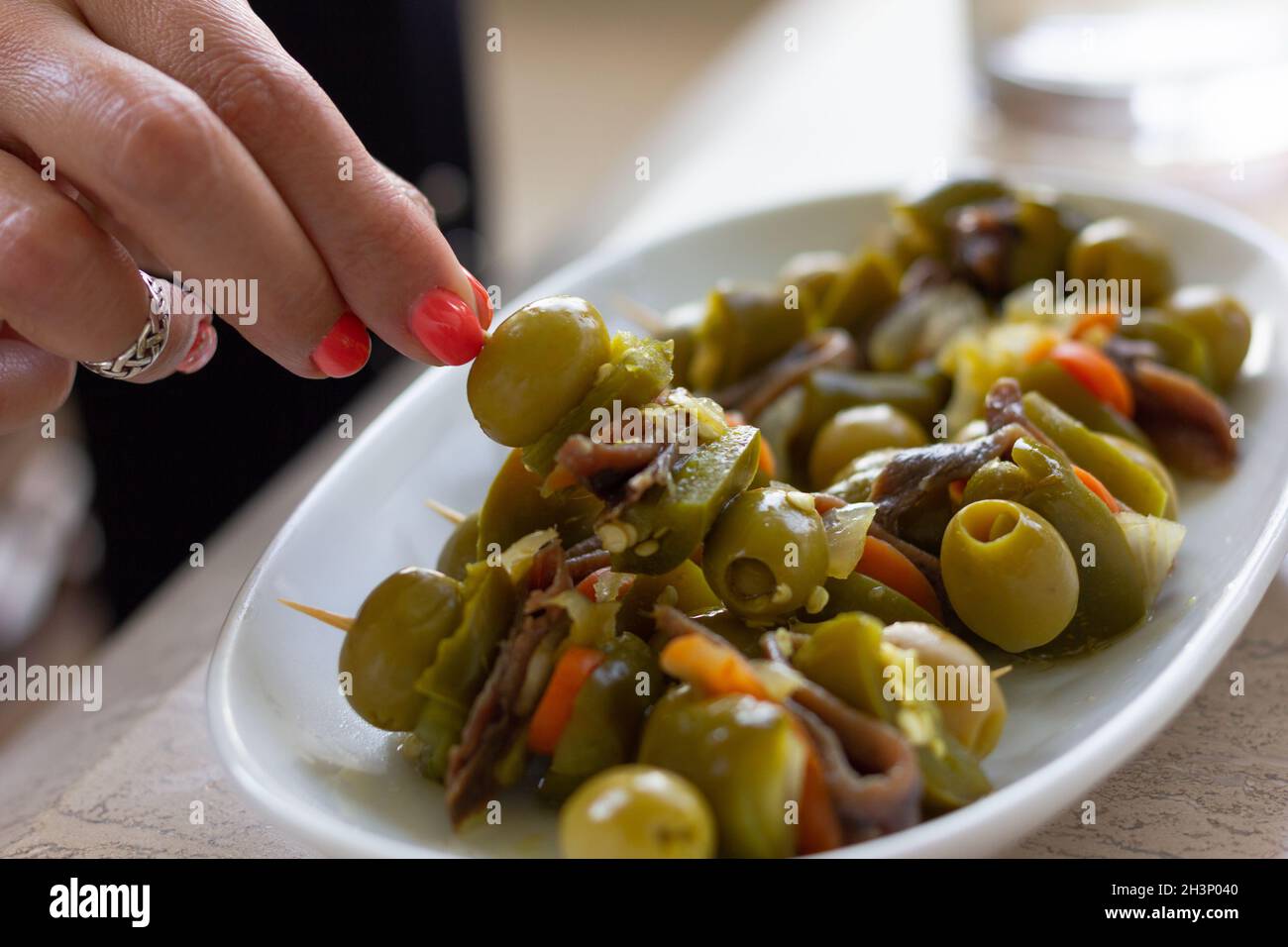 Hand of woman taking spicy skewered appetizers with green olives ...