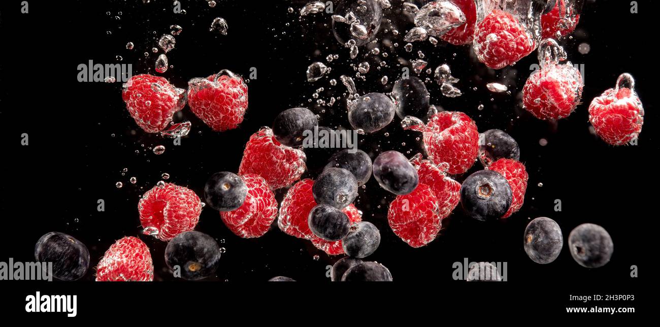 Blueberries and raspberries splashing into water with air bubbles and ...