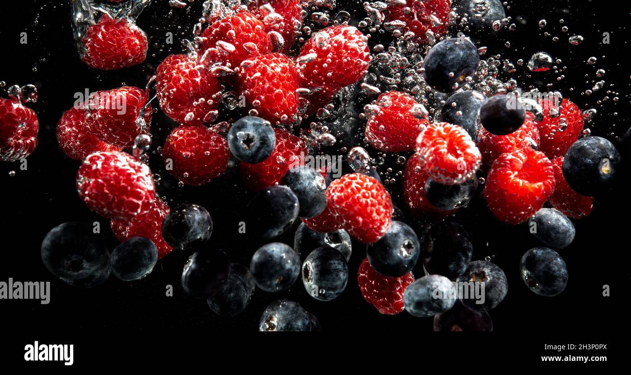 Blueberries and raspberries splashing into water with air bubbles and ...