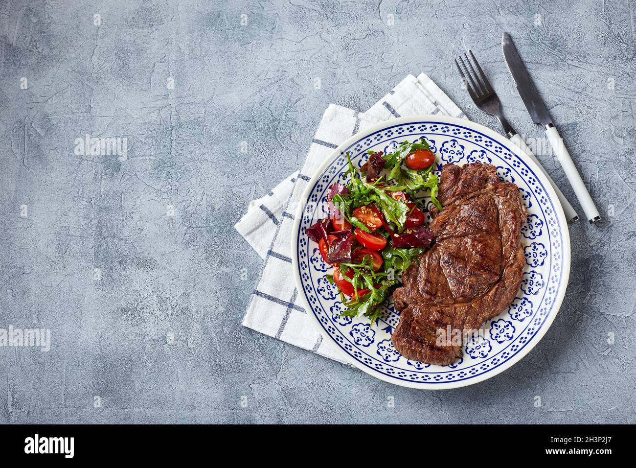 Grilled steaks and vegetable salad on light background. Table setting ...