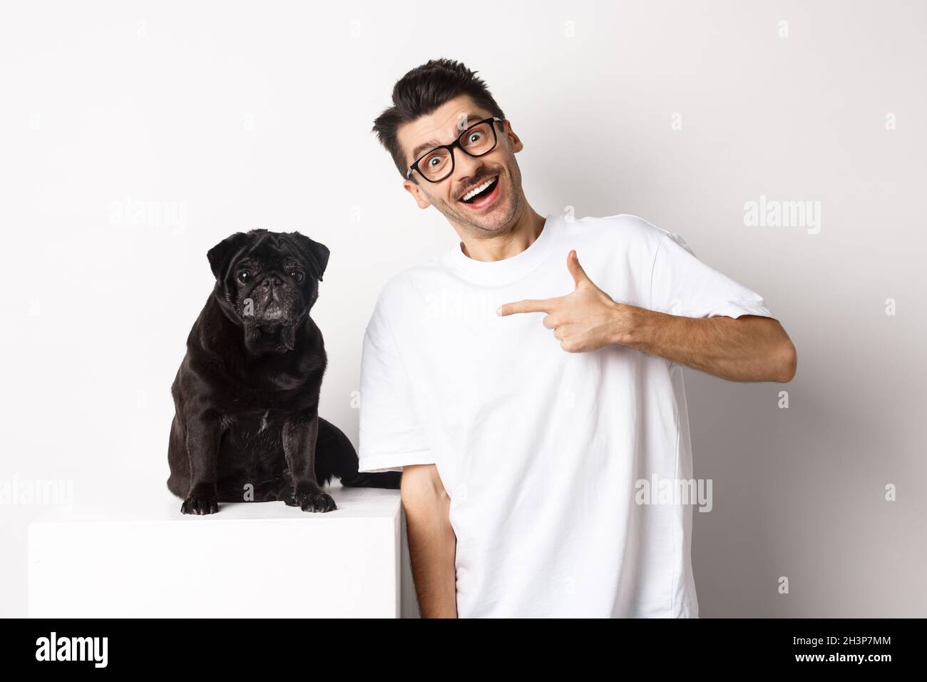 Happy young man showing his cute dog, pointing finger at black pug and ...