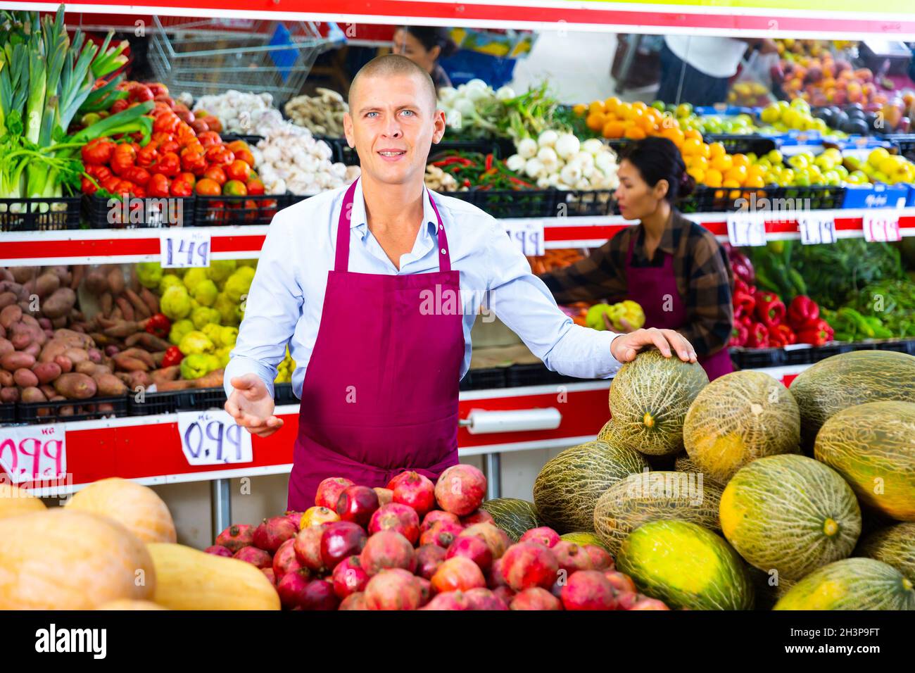 Smiling seller offering fresh fruits and vegetables in greengrocery ...