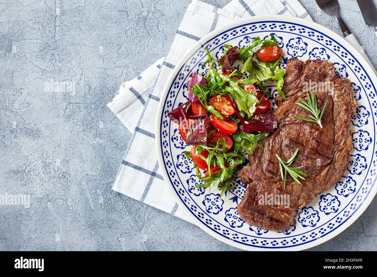 Grilled steaks and vegetable salad on light background. Table setting ...