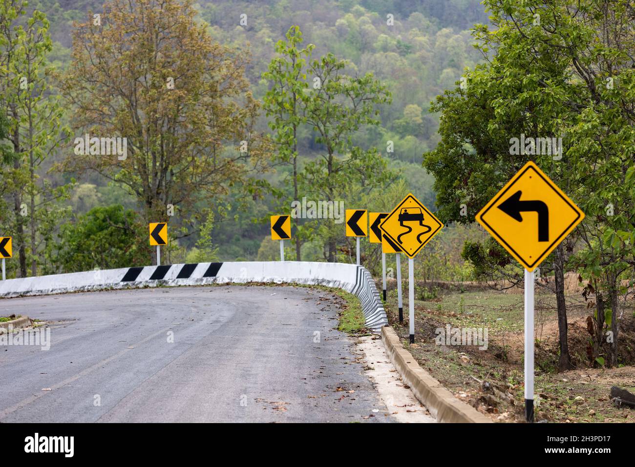 Road sign caution indicating left turn and danger of slippery road on ...