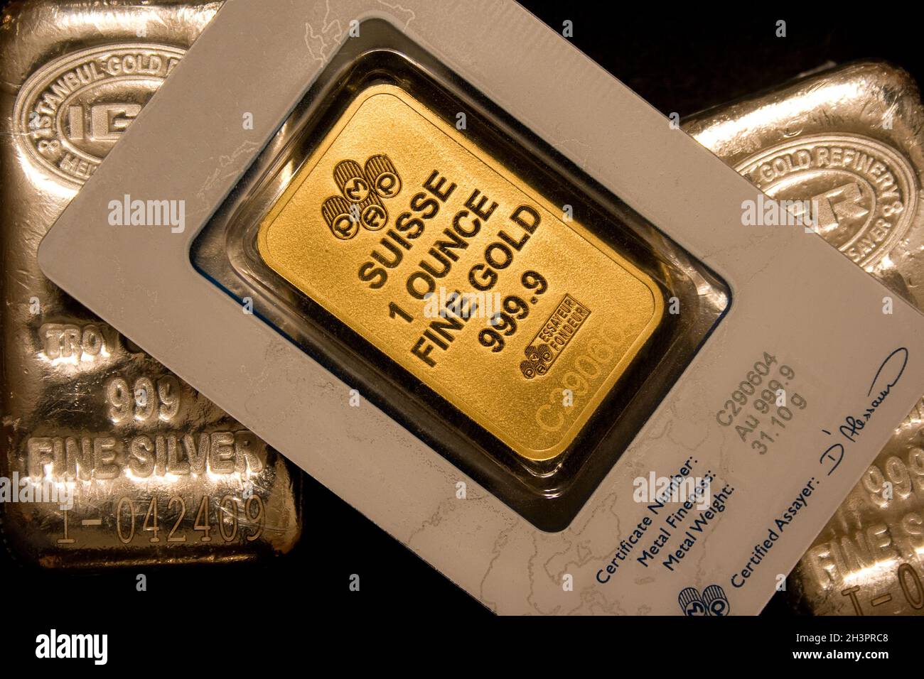 Pure One Troy Ounce Gold Bar With Assay Two Silver Bars In Background Pure One Troy Ounce Gold Bar With Assay Two Silver Bars In Background